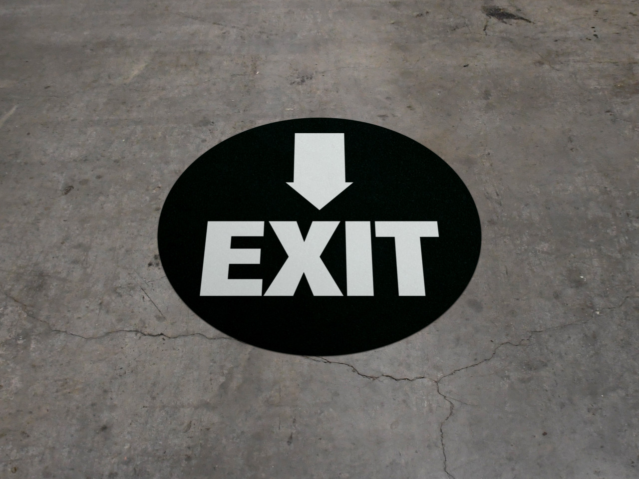 Glow: Exit Arrow Down (Black Circle) - Floor Sign | Creative Safety Supply