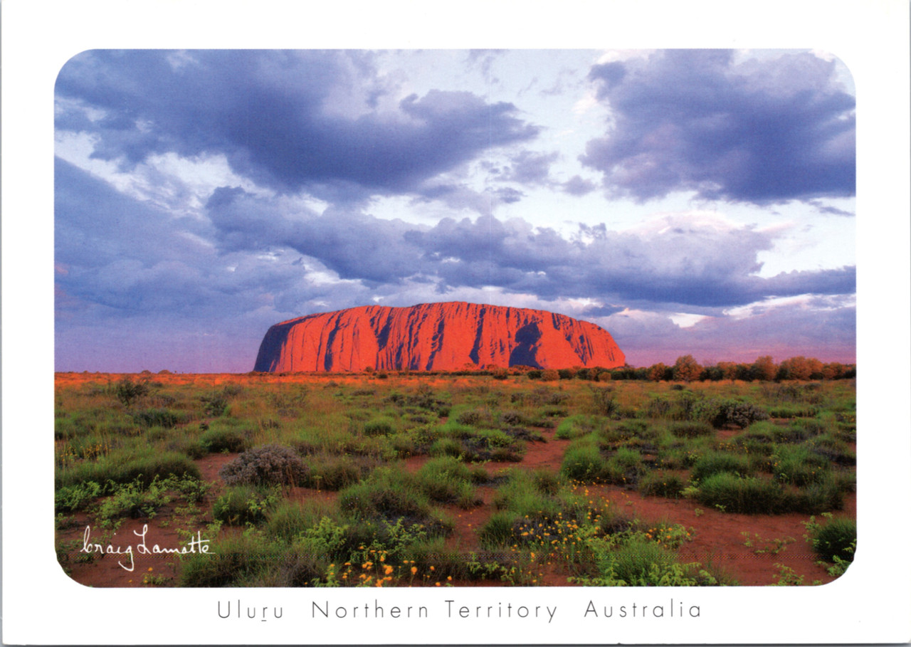 Uluru glows red by light of descending sun as storm clouds approach ...