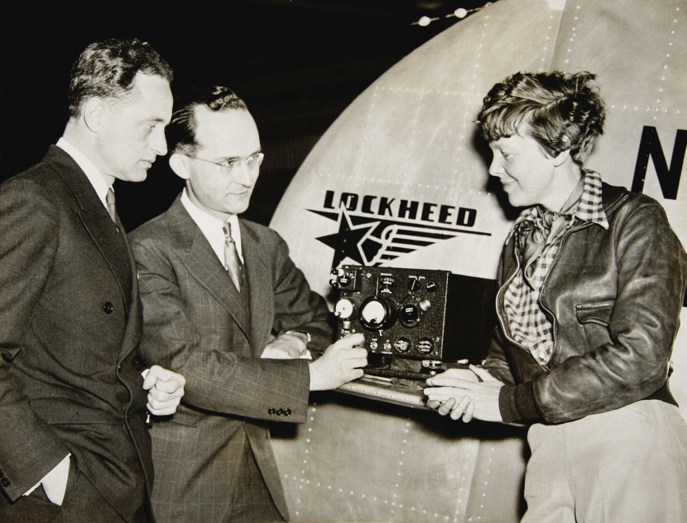 Early press photo of Amelia Earhart. Two men talk with Amelia in front ...