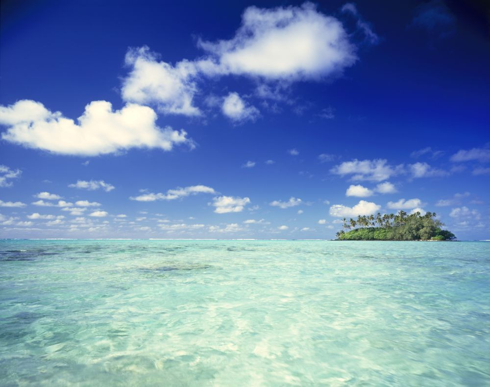 Palm trees and lush foliage cover a small island in the Cook Islands ...