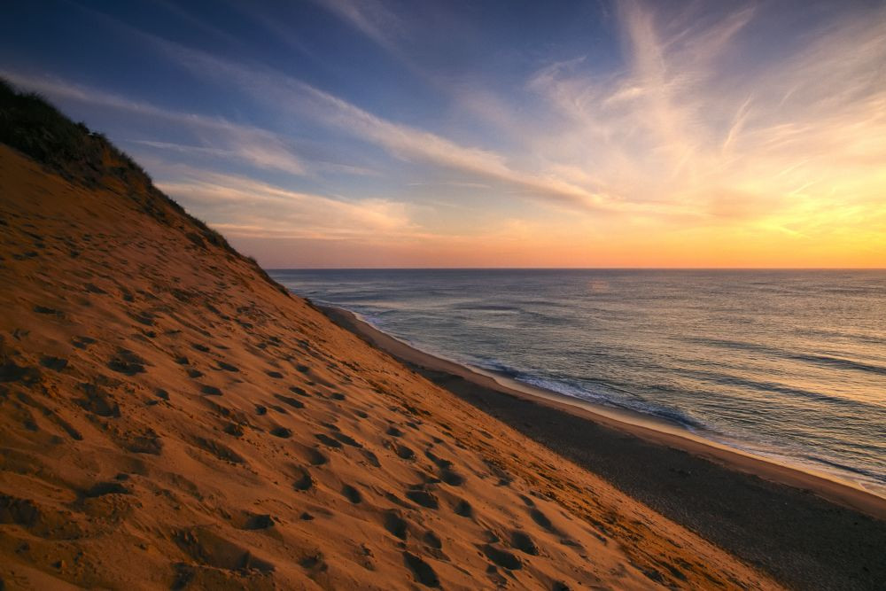 Sunrise paints the sky orange over the shoreline of Coastguard Beach ...